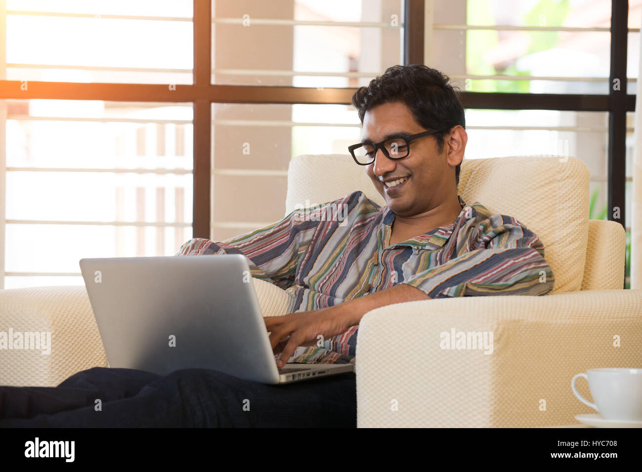 casual indian male using computer on sofa Stock Photo - Alamy