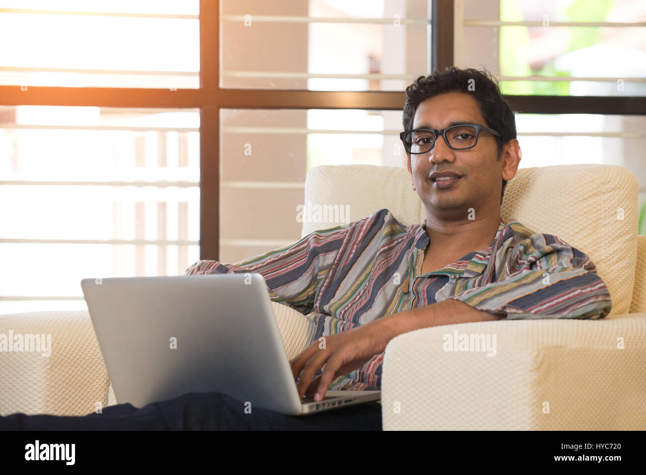casual indian male using computer on sofa Stock Photo - Alamy