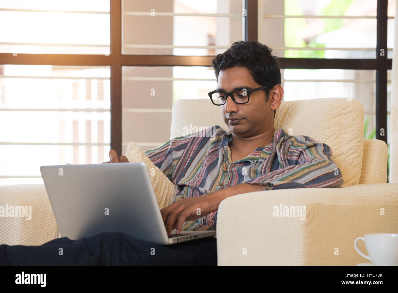 casual indian male using computer on sofa Stock Photo - Alamy
