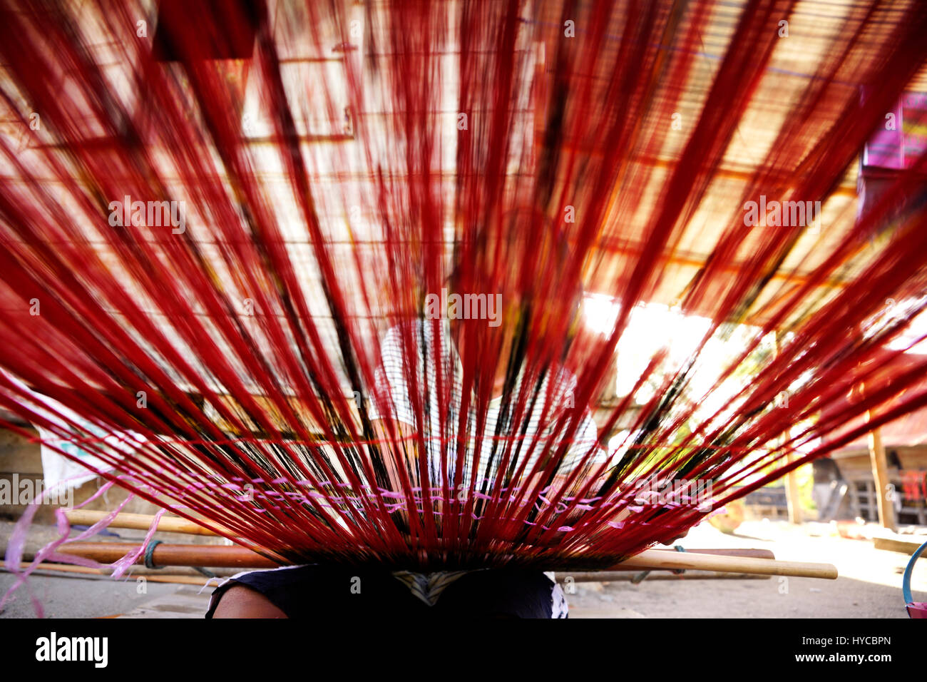 Woman weaving red threads with hands on weaving device seen from a low ...