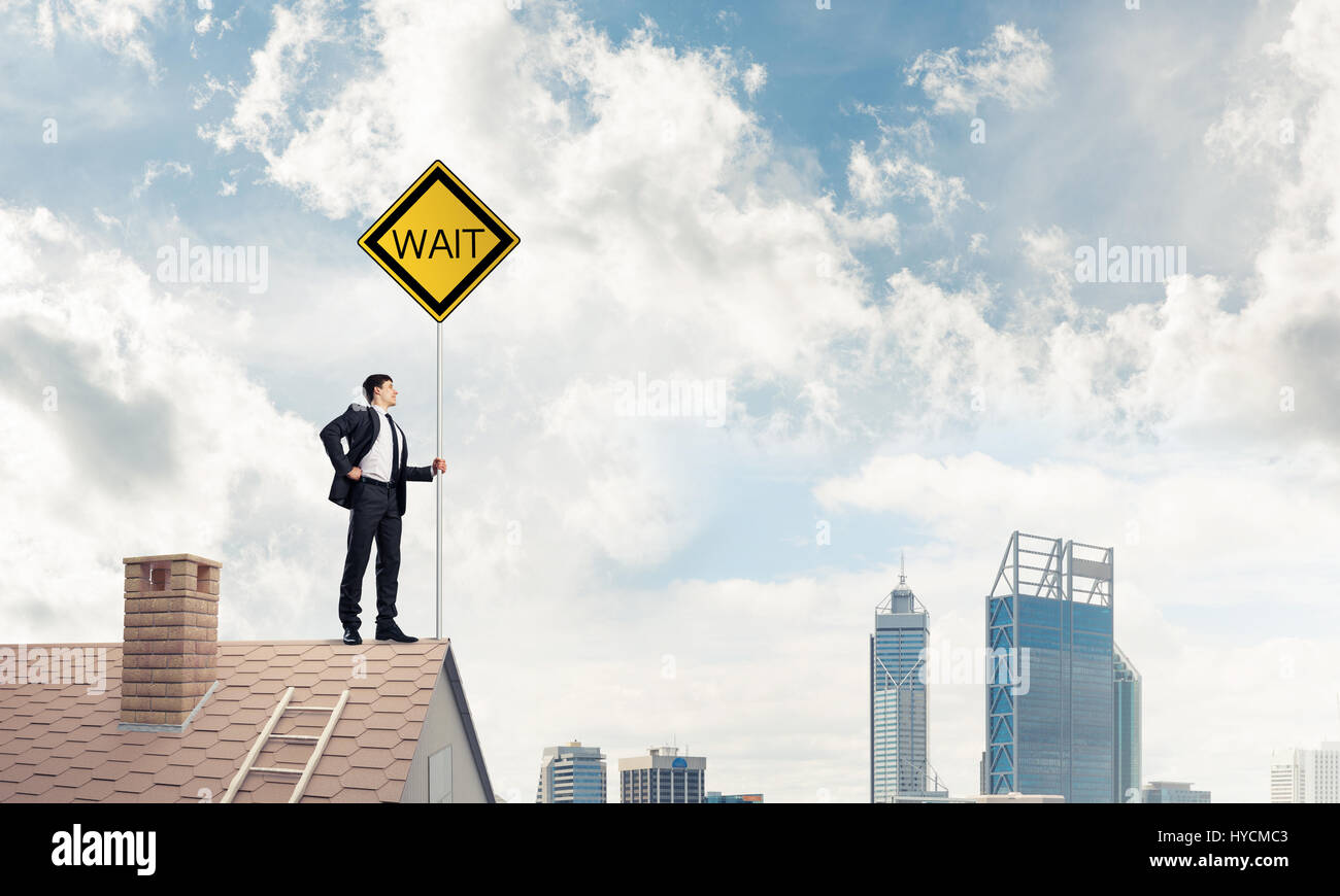 Young businessman on house brick roof holding yellow signboard a Stock ...