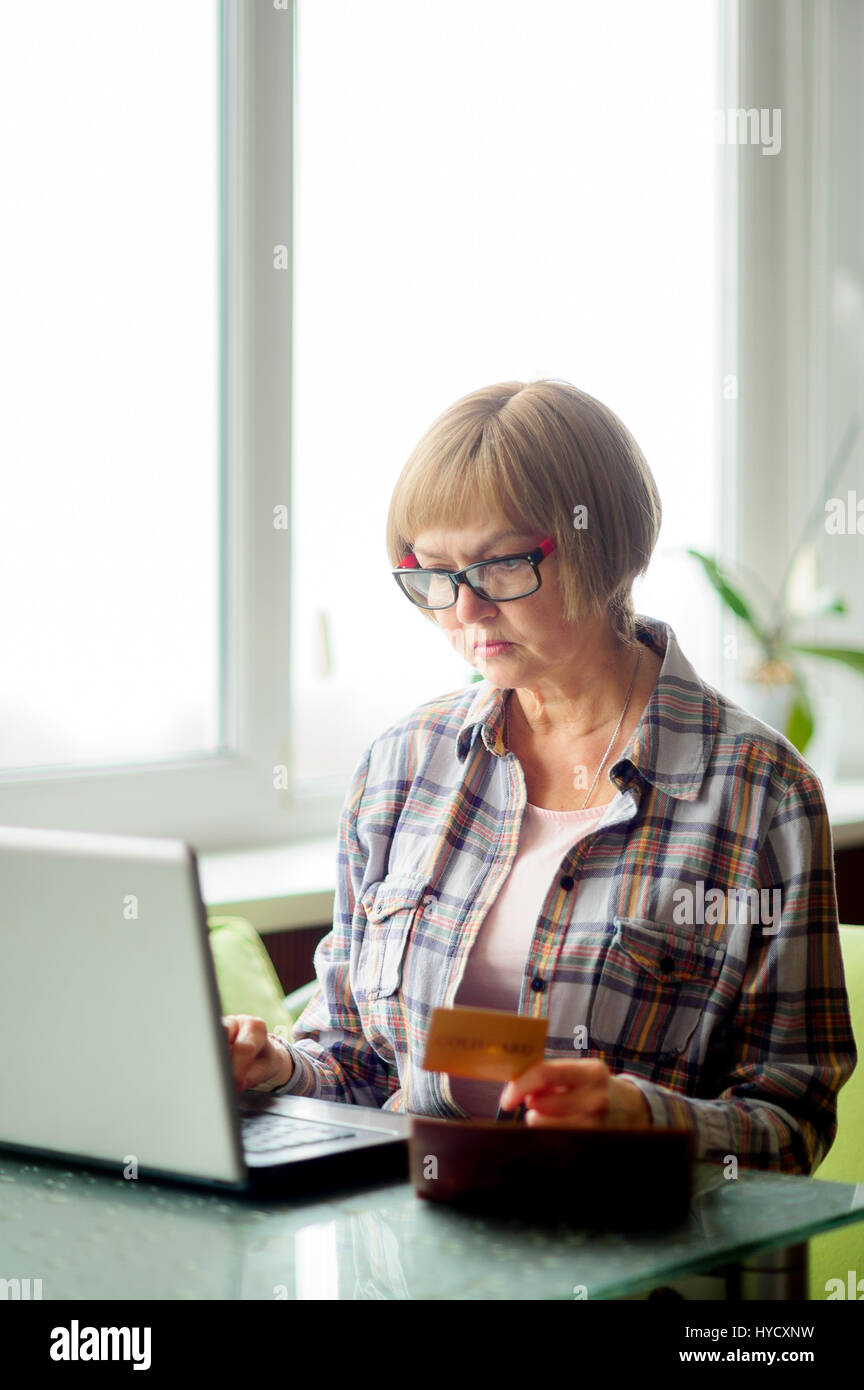 The elderly woman looks in the laptop screen. She uses the computer for ...