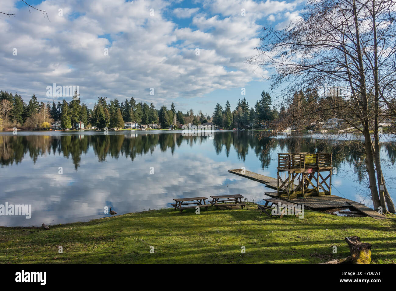 Homes, trees and sky are reflected in the water of Mirror Lake in ...