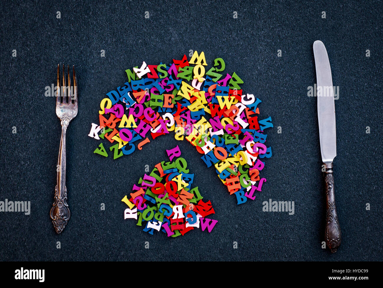 Cutlery and multicolored letters of wood on a black surface, top view ...