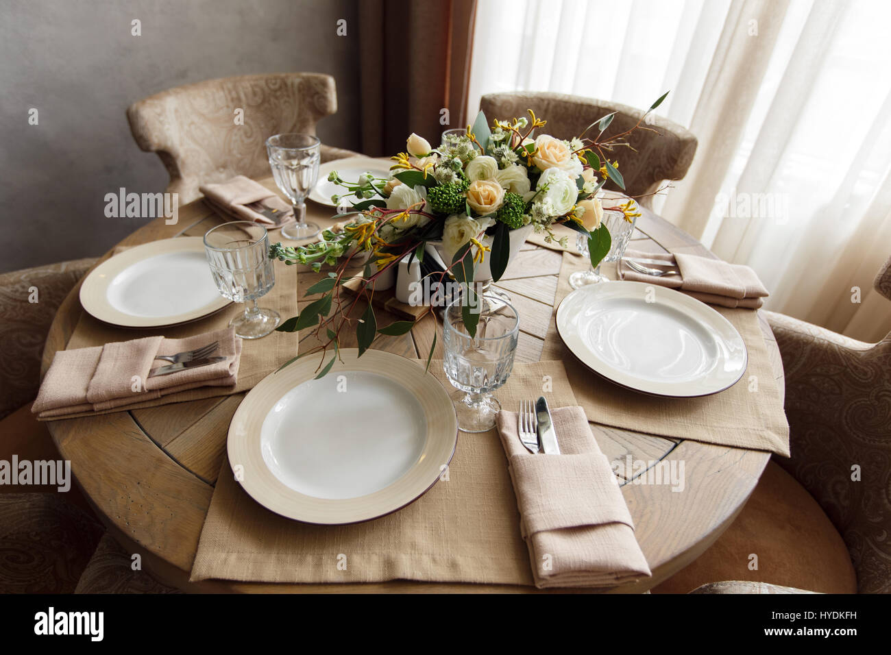 Round wooden dining table decorated with bouquet of roses and greenery ...