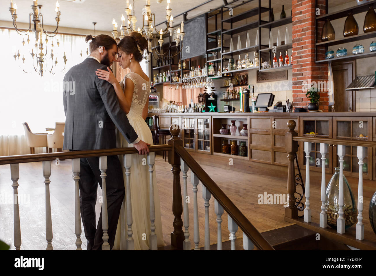 Portrait of the newlyweds from behind standing at a railing in interior ...