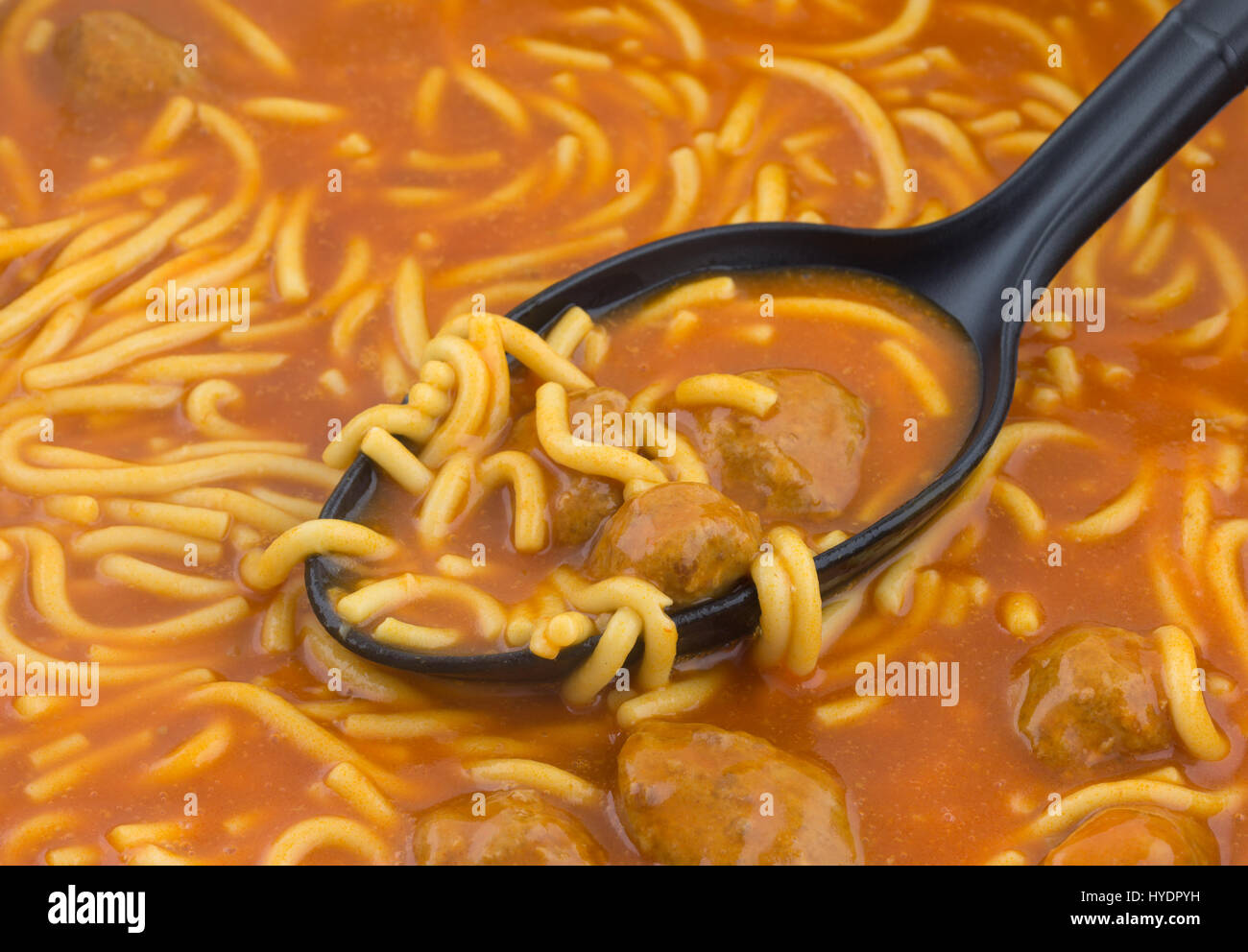 Cooking canned spaghetti and meatballs in a skillet with a black spoon ...