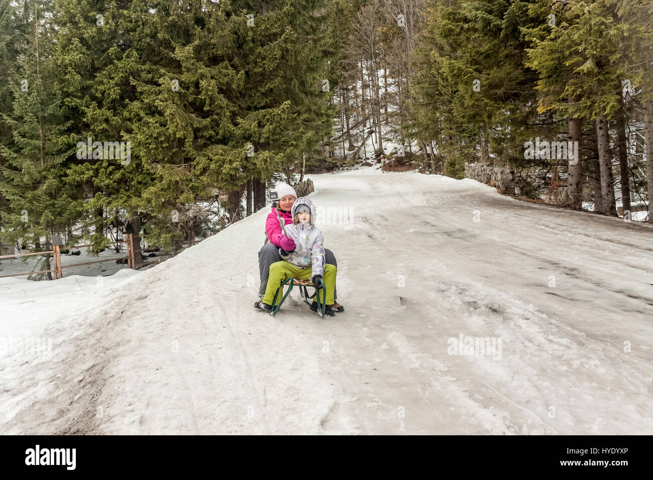 Woman filming with action camera while riding sled with her daughter ...