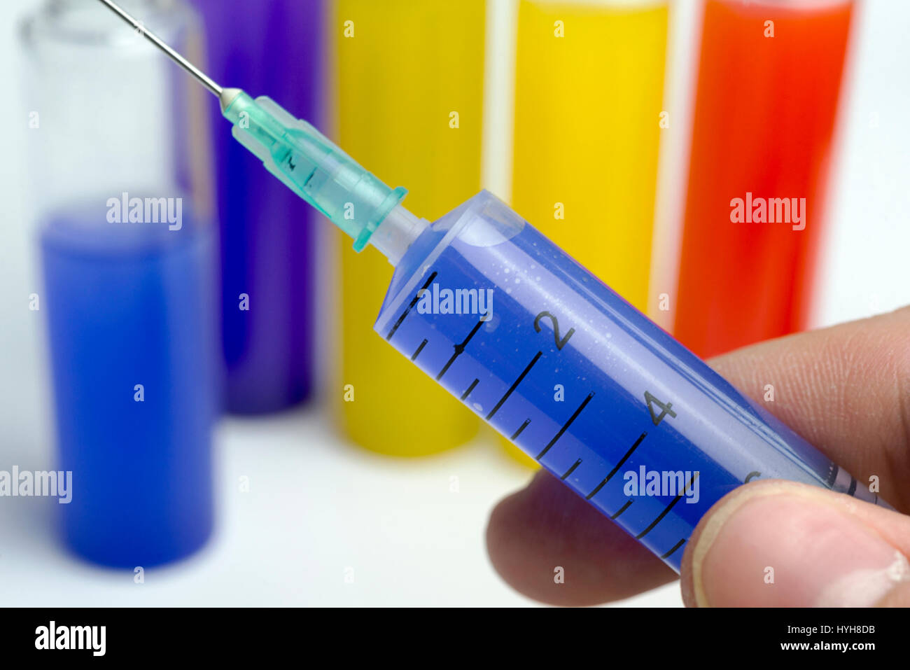Hand holding test tube with blue liquid and a syringe on a white ...