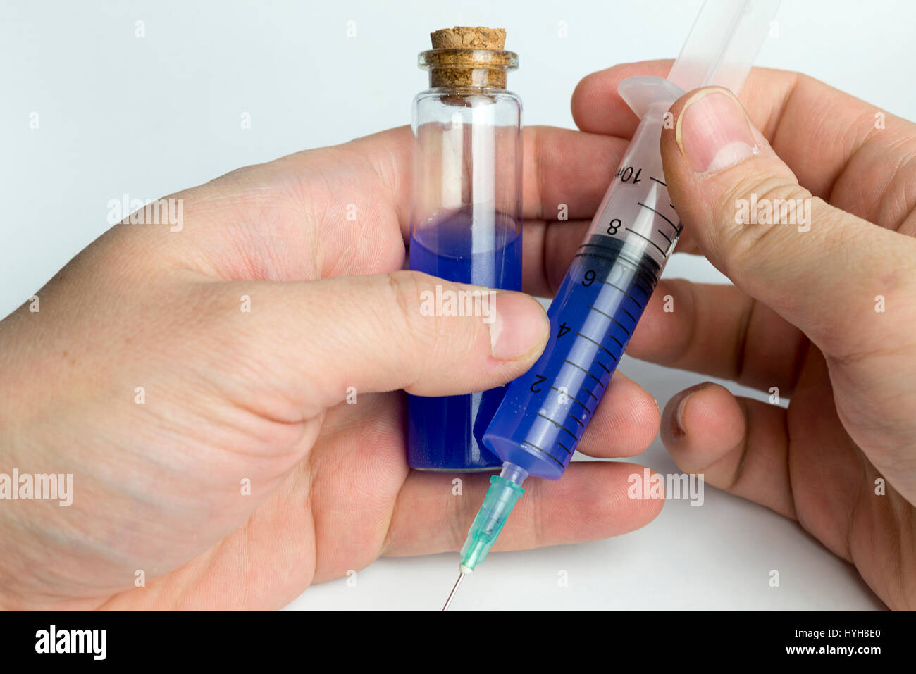 Hand holding test tube with blue liquid and a syringe on a white ...