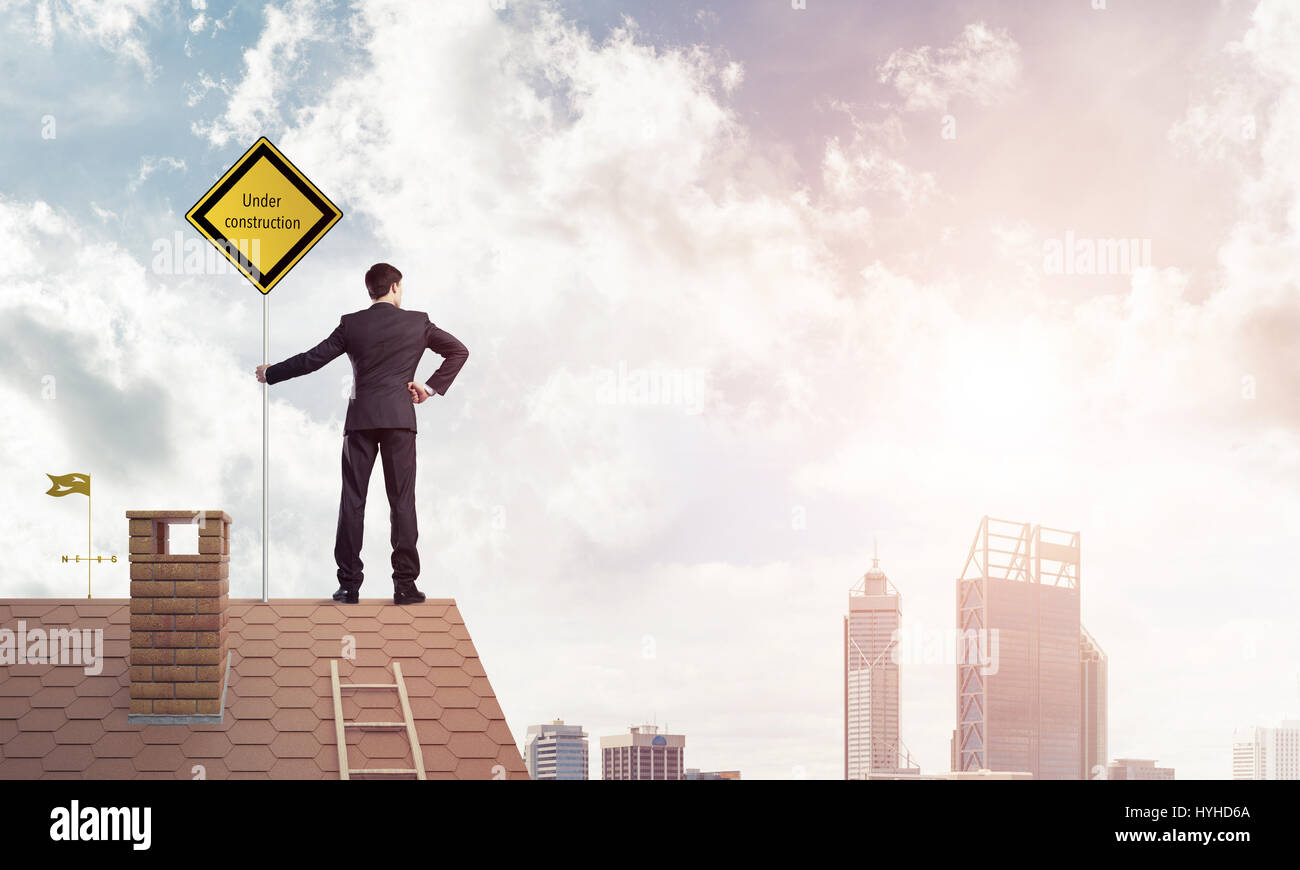 Young businessman on house brick roof holding yellow signboard a Stock ...