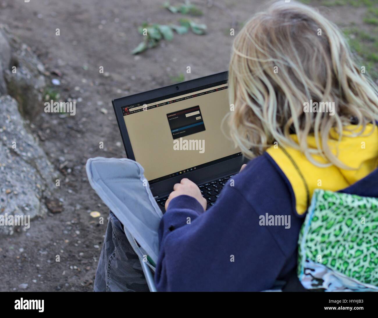 Boy using a laptop technology outdoors around an empty campfire. Model ...