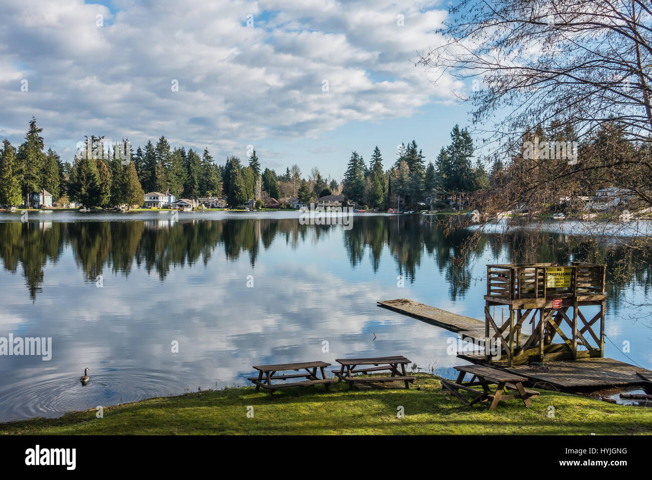 Homes, trees and sky are reflected in the water of Mirror Lake in ...