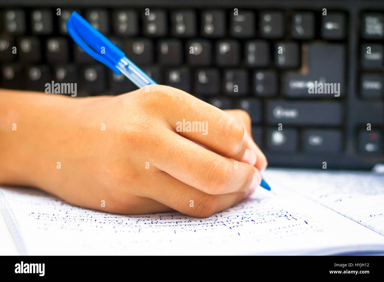 Human hand holding pen on white paper with keyboard in the back ground ...