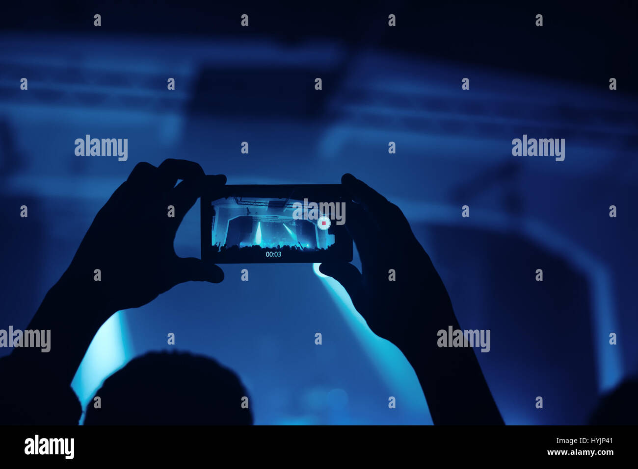 Hands with smartphone recording footage on live rock concert, selective ...