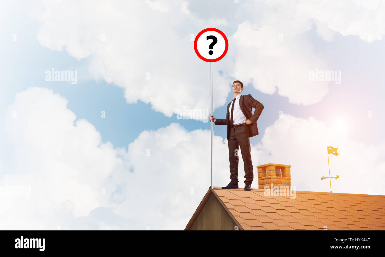 Businessman on brick house roof showing banner with question mark ...