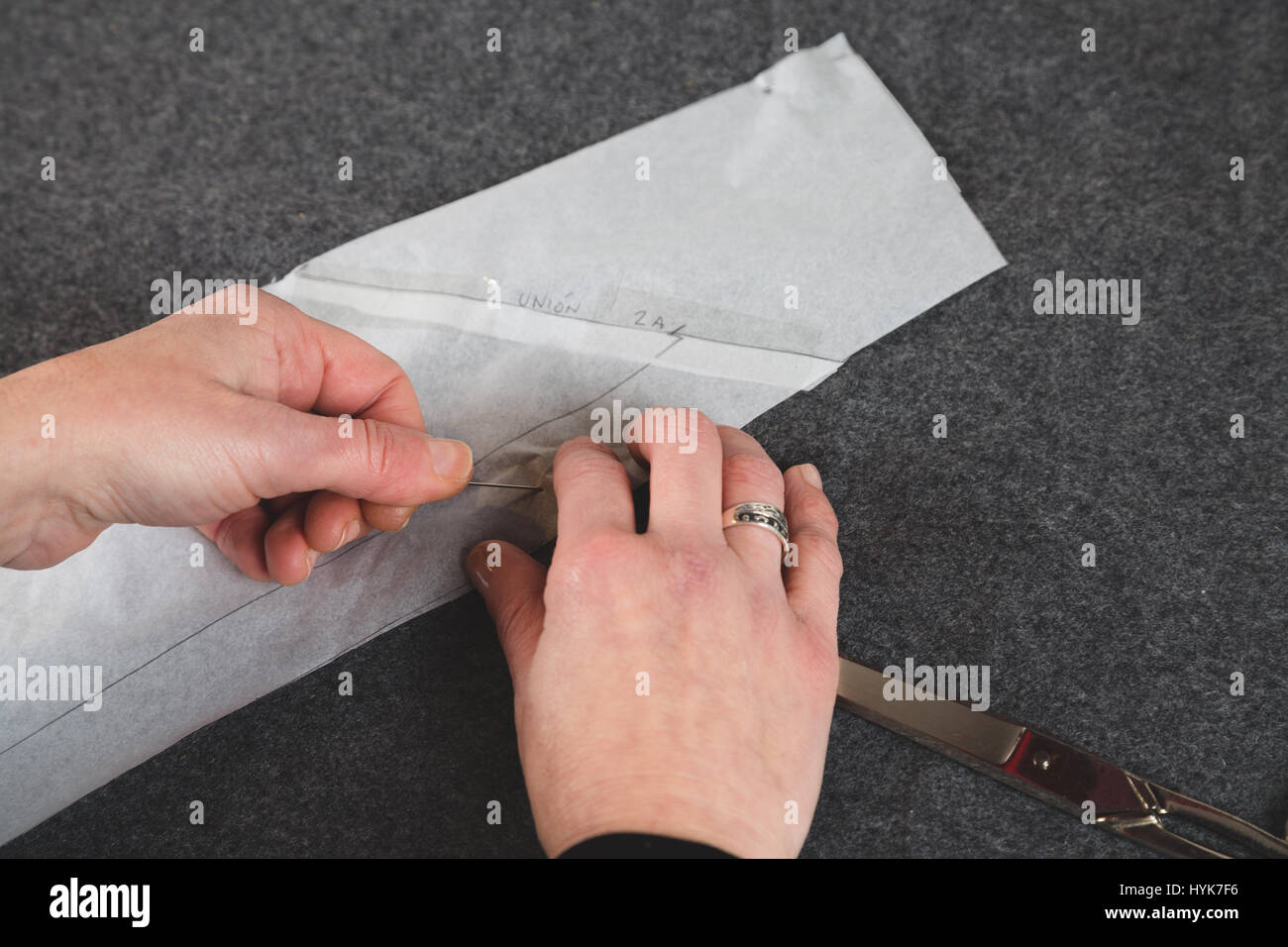 Hands of seamstress fixing paper template with pins to grey fabric ...