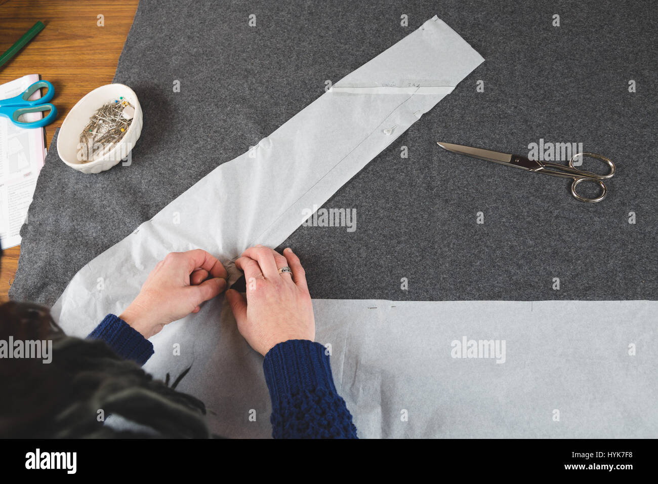 Hands of seamstress fixing paper template with pins to grey fabric ...