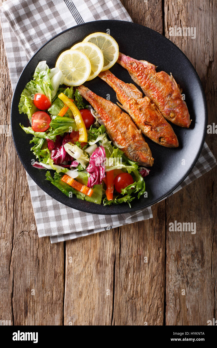 Roasted red mullet with fresh vegetables and lemon close-up on a plate ...