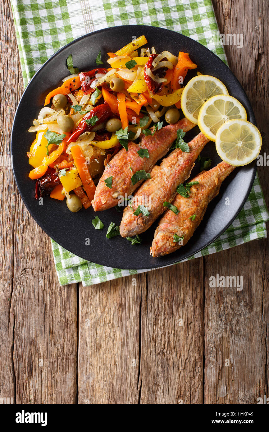 Roasted red mullet with stewed vegetables, lemon and greens close-up on ...
