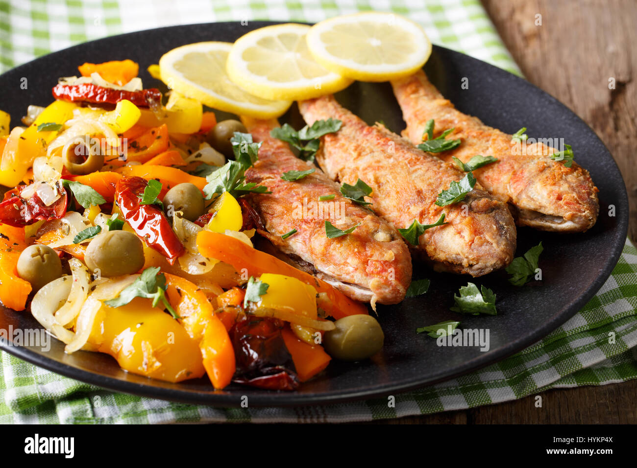 Roasted red mullet with stewed vegetables, lemon and greens close-up on ...