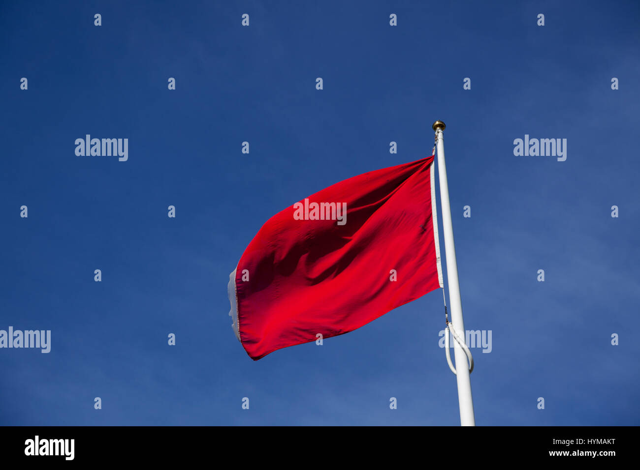 Red WArning Flag Flying Against Blue Sky Stock Photo - Alamy