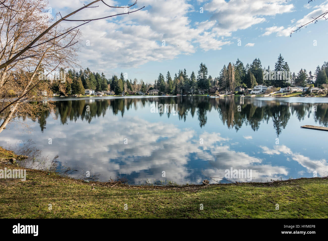 Homes, trees and sky are reflected in the water of Mirror Lake in ...