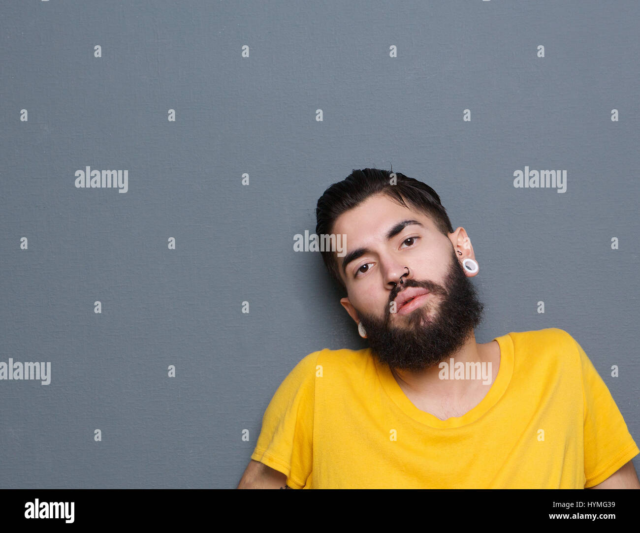 Portrait of a latin man with beard and piercings posing on gray ...
