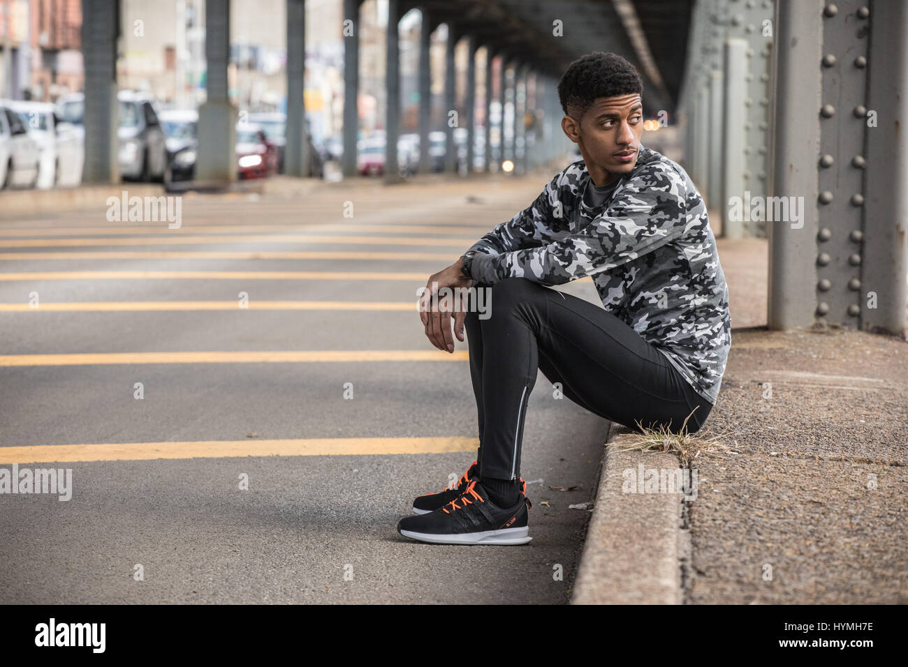 A portrait of a young man in gym clothes sitting on the curb. Shot ...