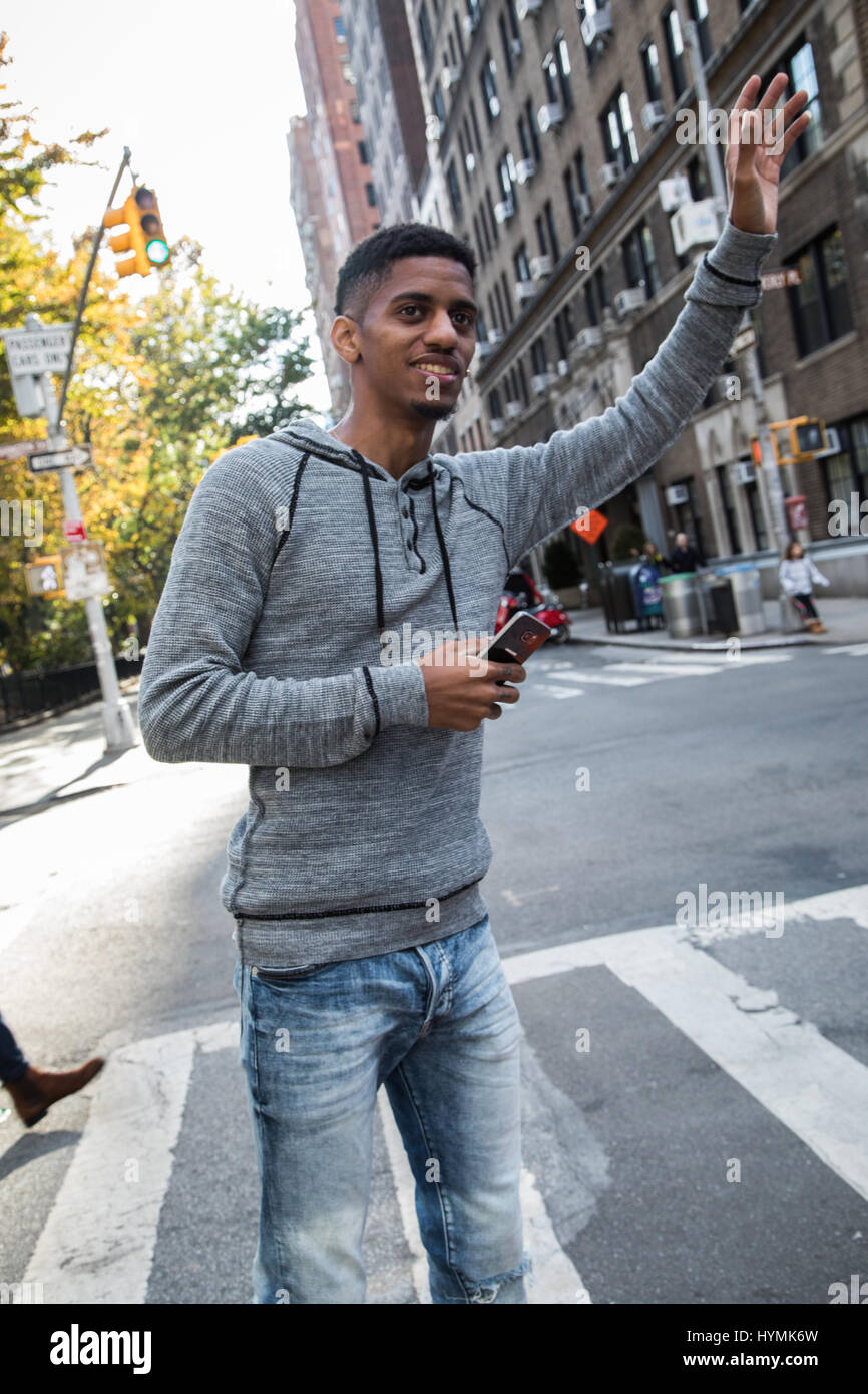 A portrait of a happy, young man hailing a cab in NYC. Shot during the ...