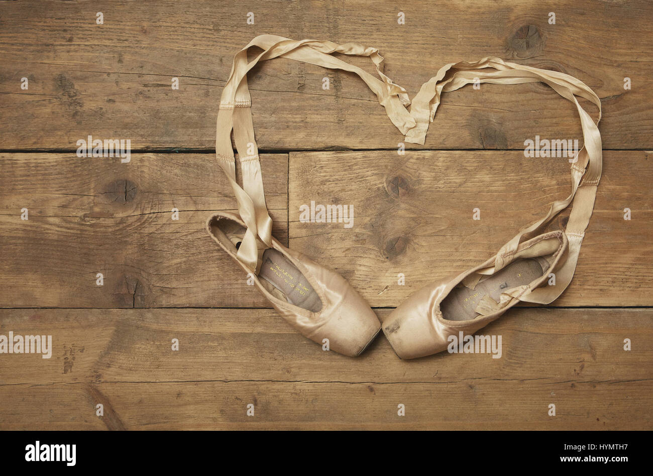 Two ballet shoes on wooden floor with ribbon in heart shape - above ...