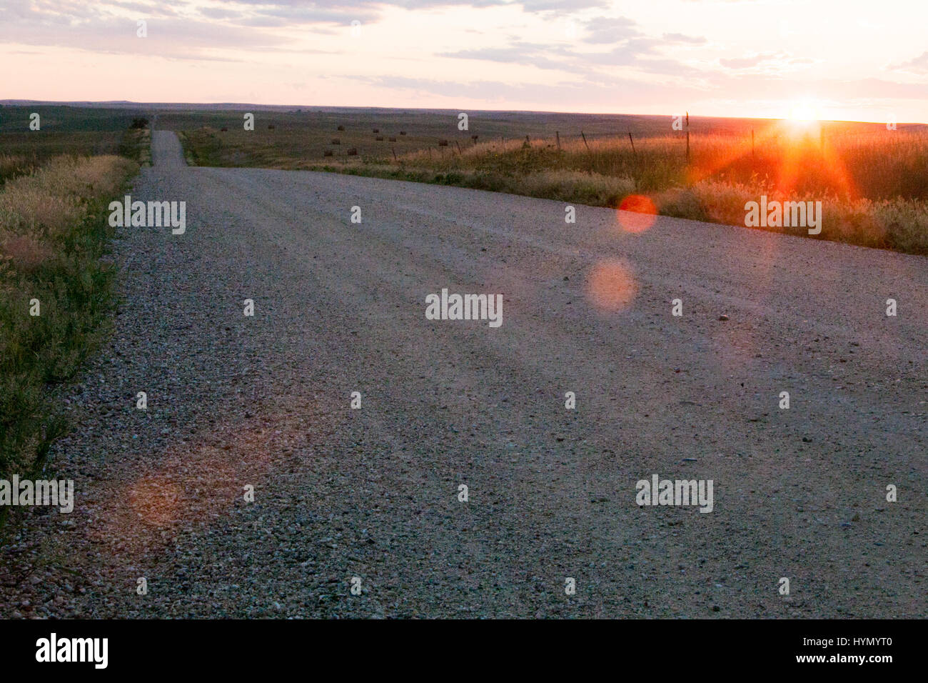 The sun sets on the horizon near a long, open country road Stock Photo ...