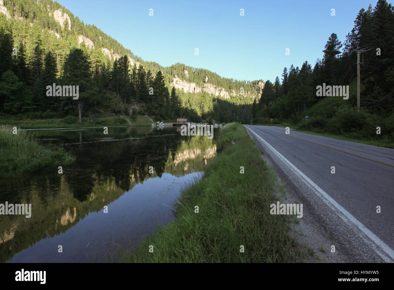A stream runs parallel open road at the base of a mountain valley Stock ...