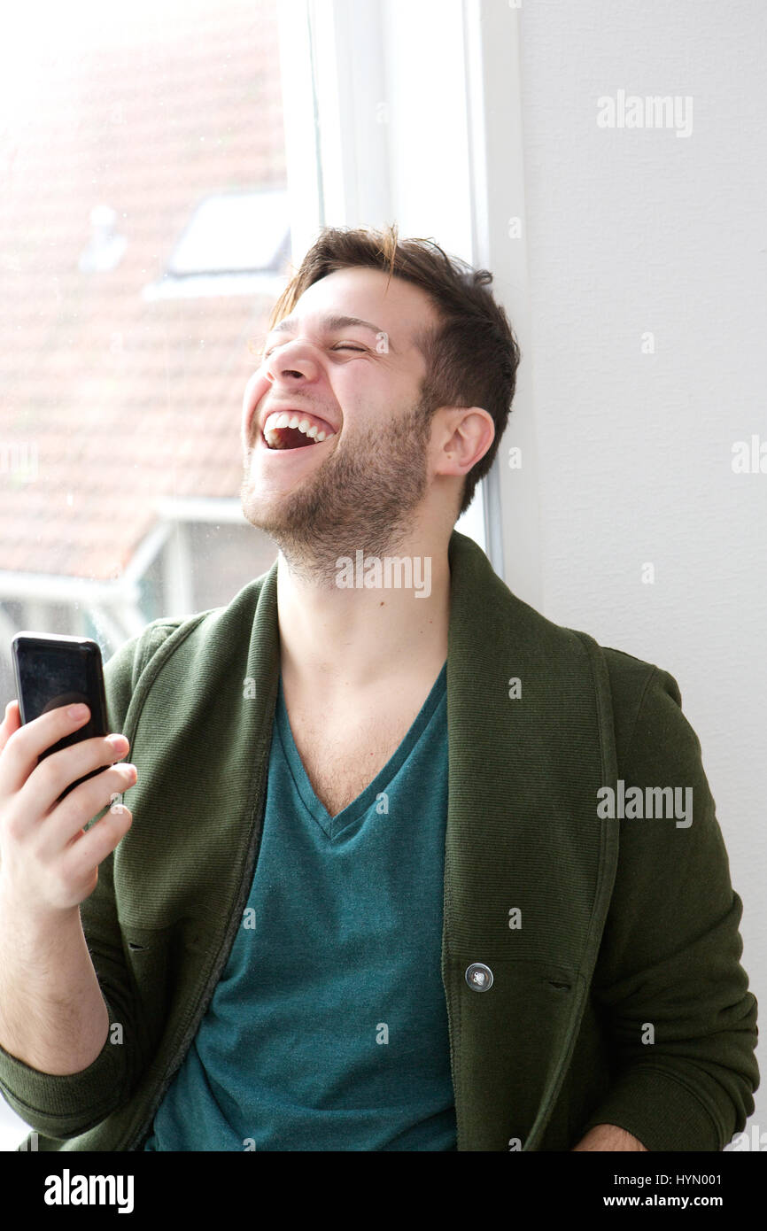 Portrait of a handsome young man laughing with mobile phone at home ...