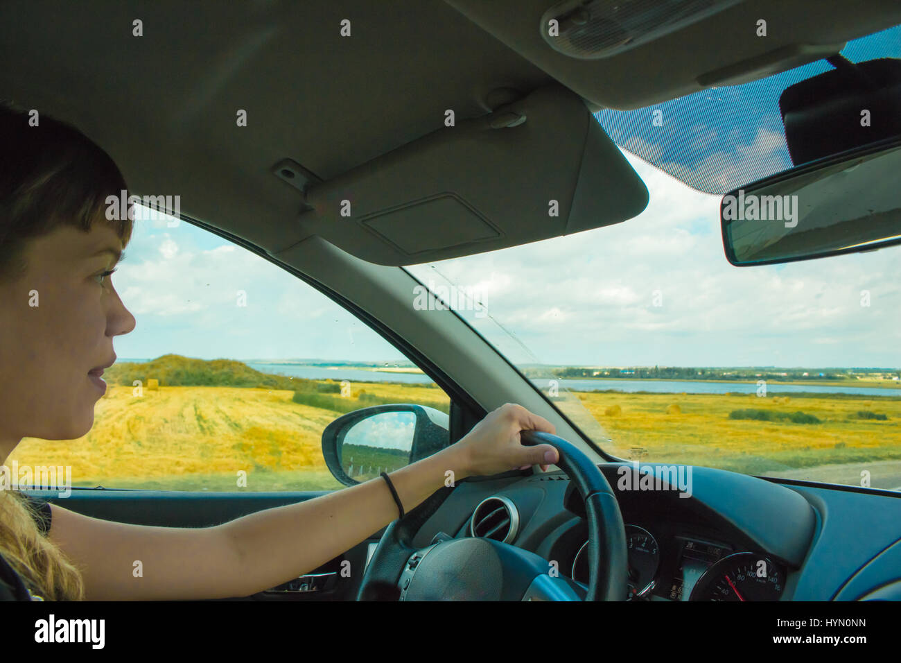 Woman driving car hand on handlebars, green fields and sea on bright ...