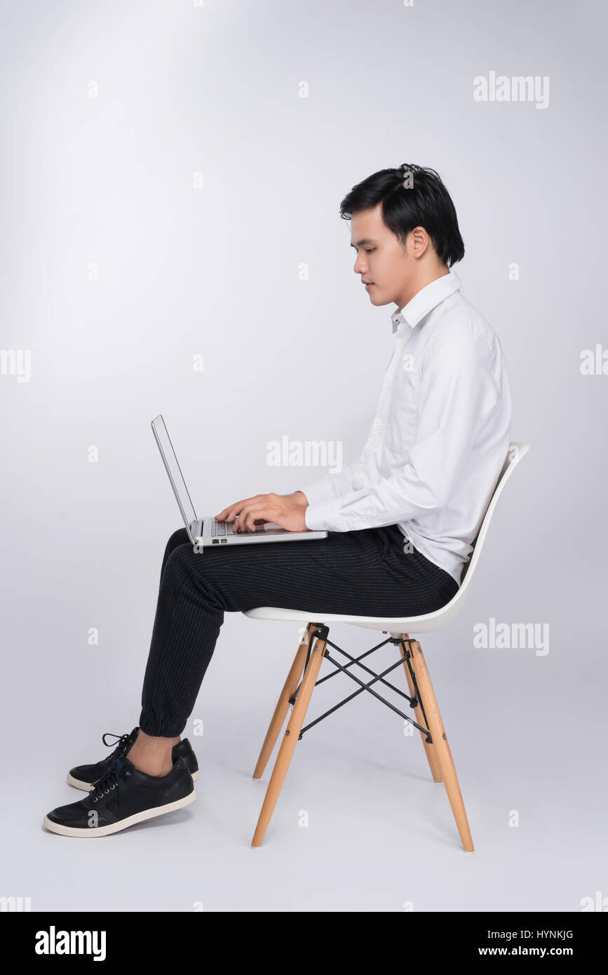 Smart casual asian man seated on chair, using laptop in studio ...