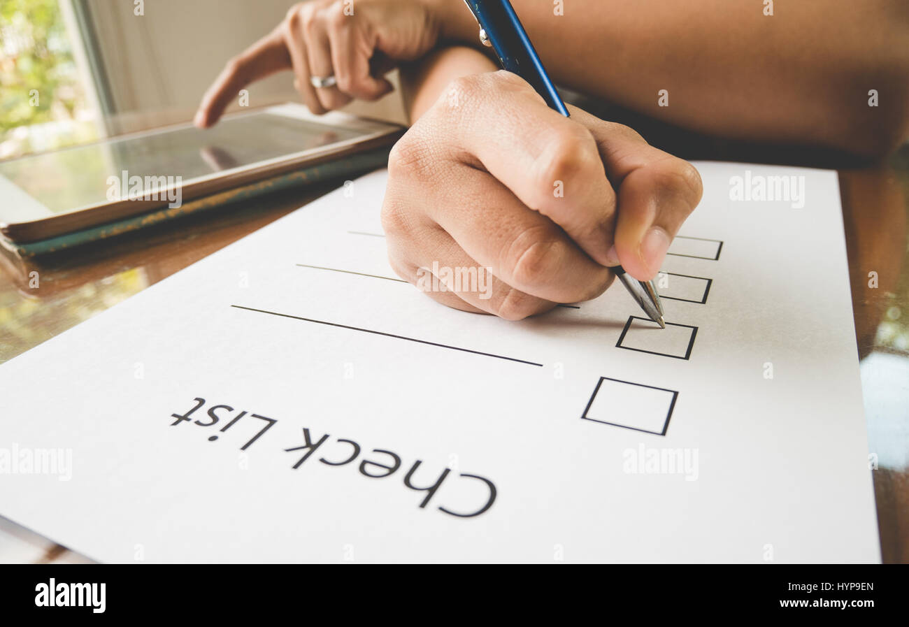 close- up hand holding pen on check list paper with tablet in vintage ...