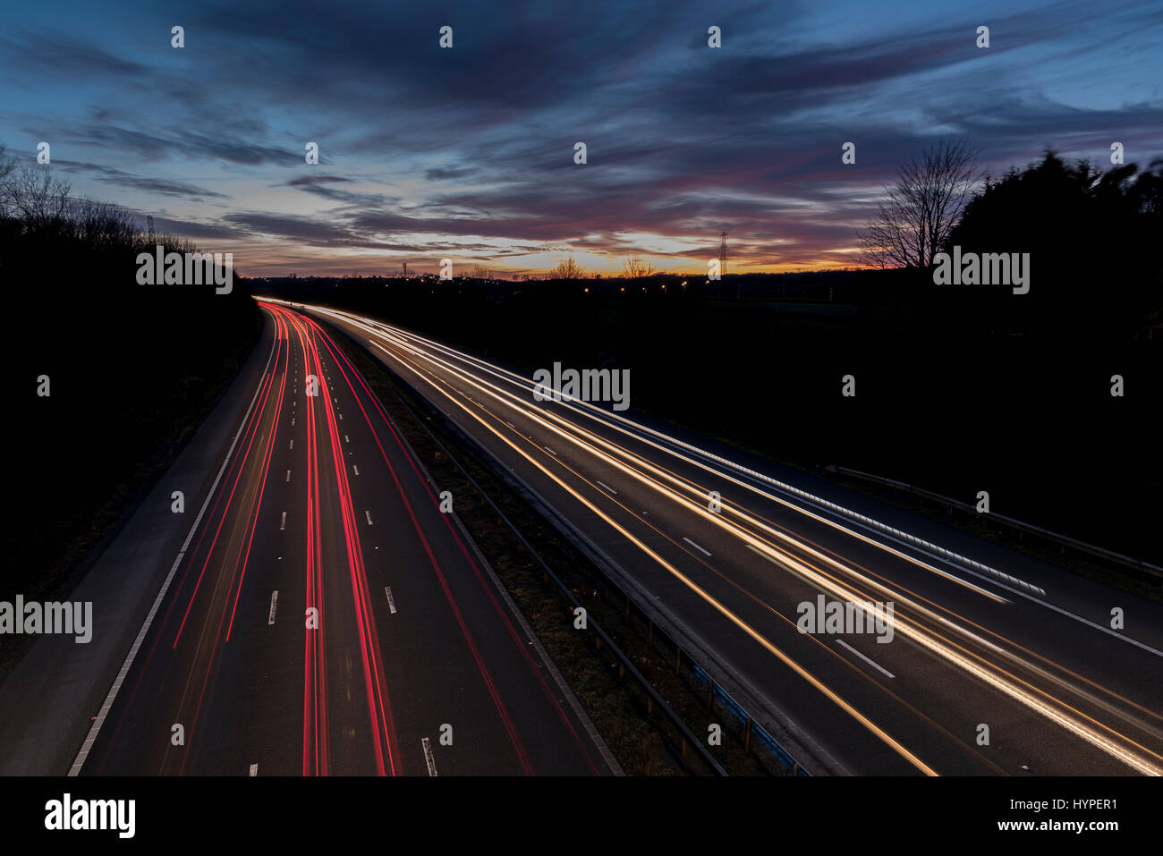 A UK motorway, at sunset, with light trails created by the traffic on ...