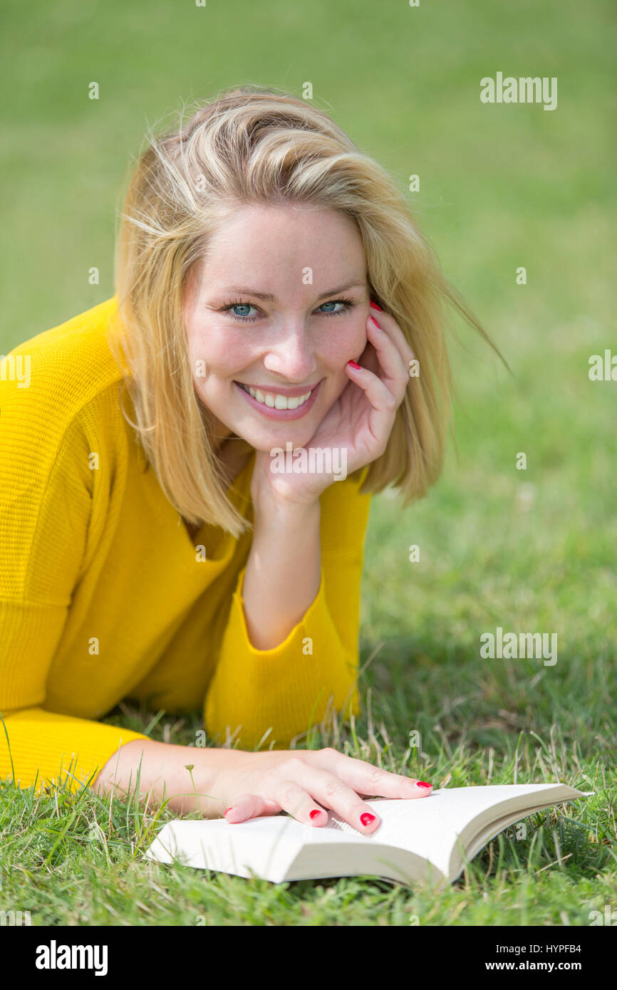 Blonde pretty woman reading a book in park smiling at camera Stock ...