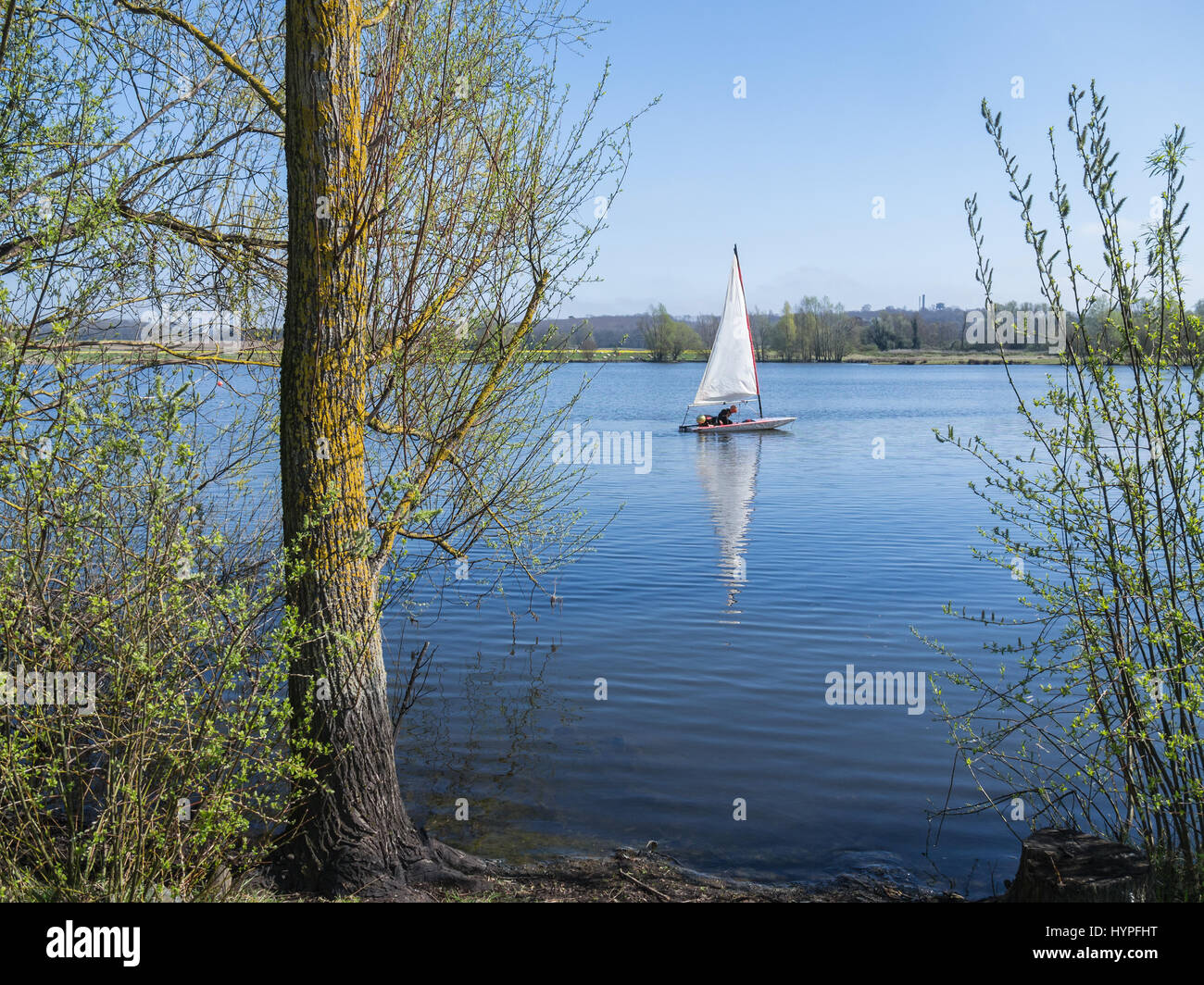 A sailing dinghy and its reflection on a peaceful blue lake ...