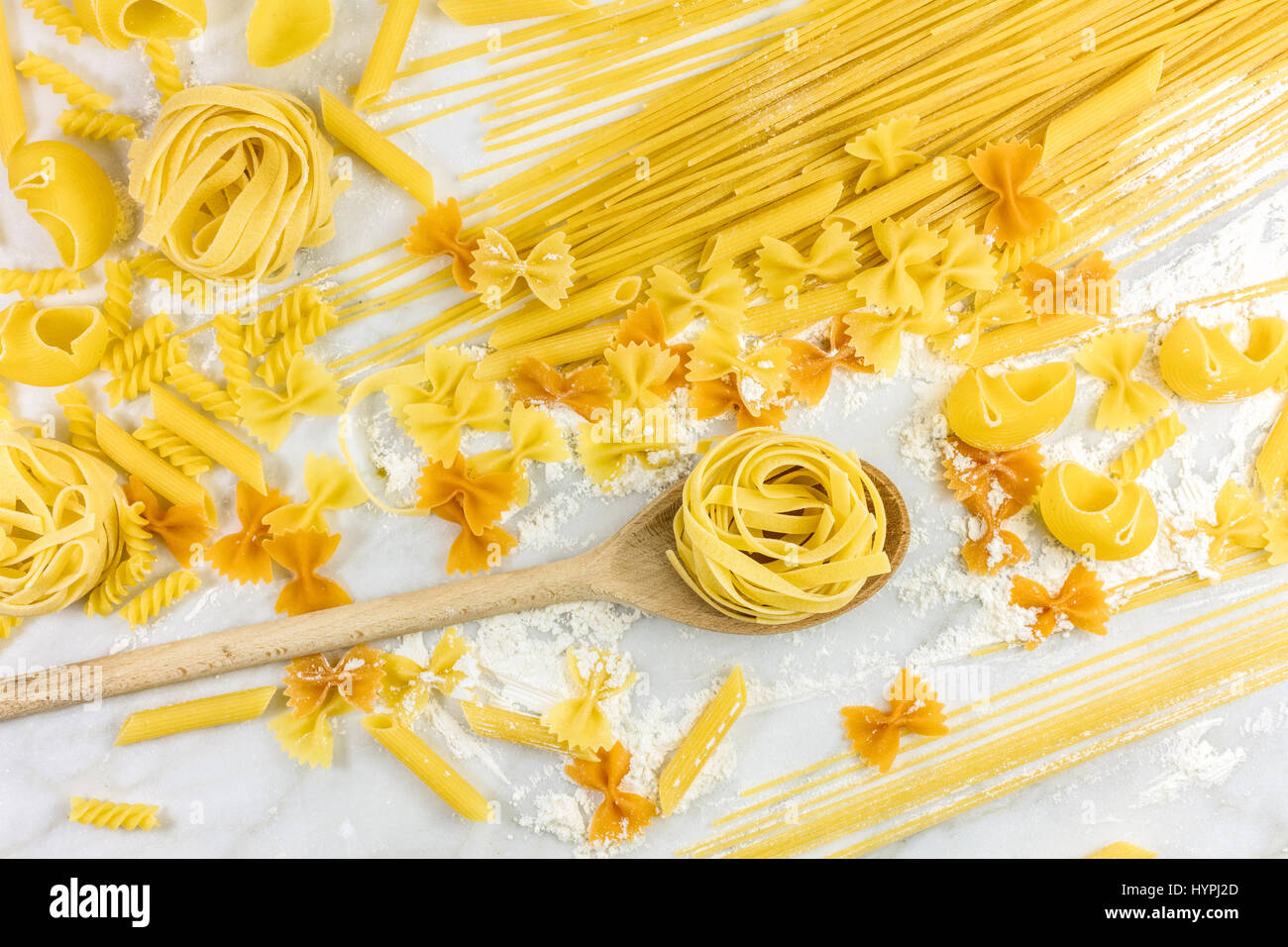 Various types of pasta on a white marble table with flour, shot from ...