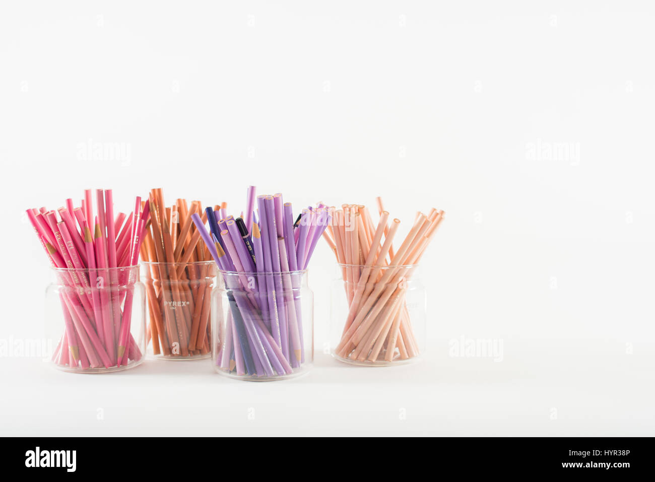 Glass containers holding coloured pencils on a white background Stock ...