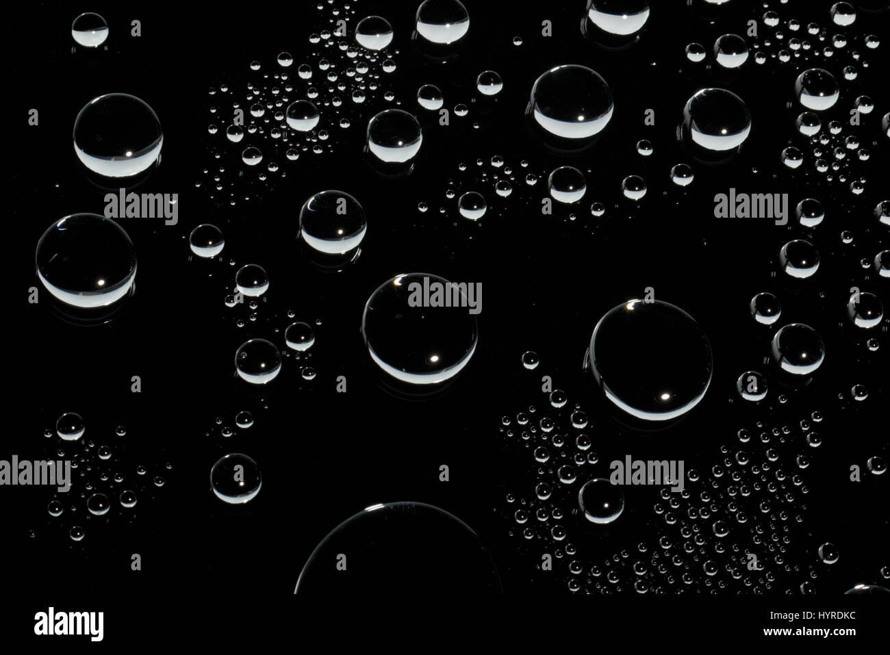 Round shaped water droplets on glass surface. Dark background behind ...