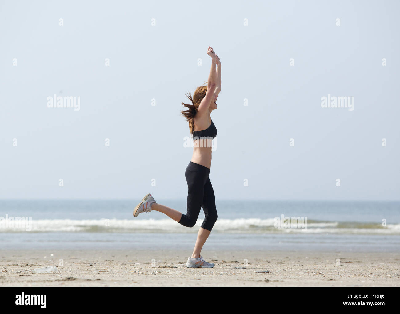 Woman running on the beach celebrating with arms raised in success ...