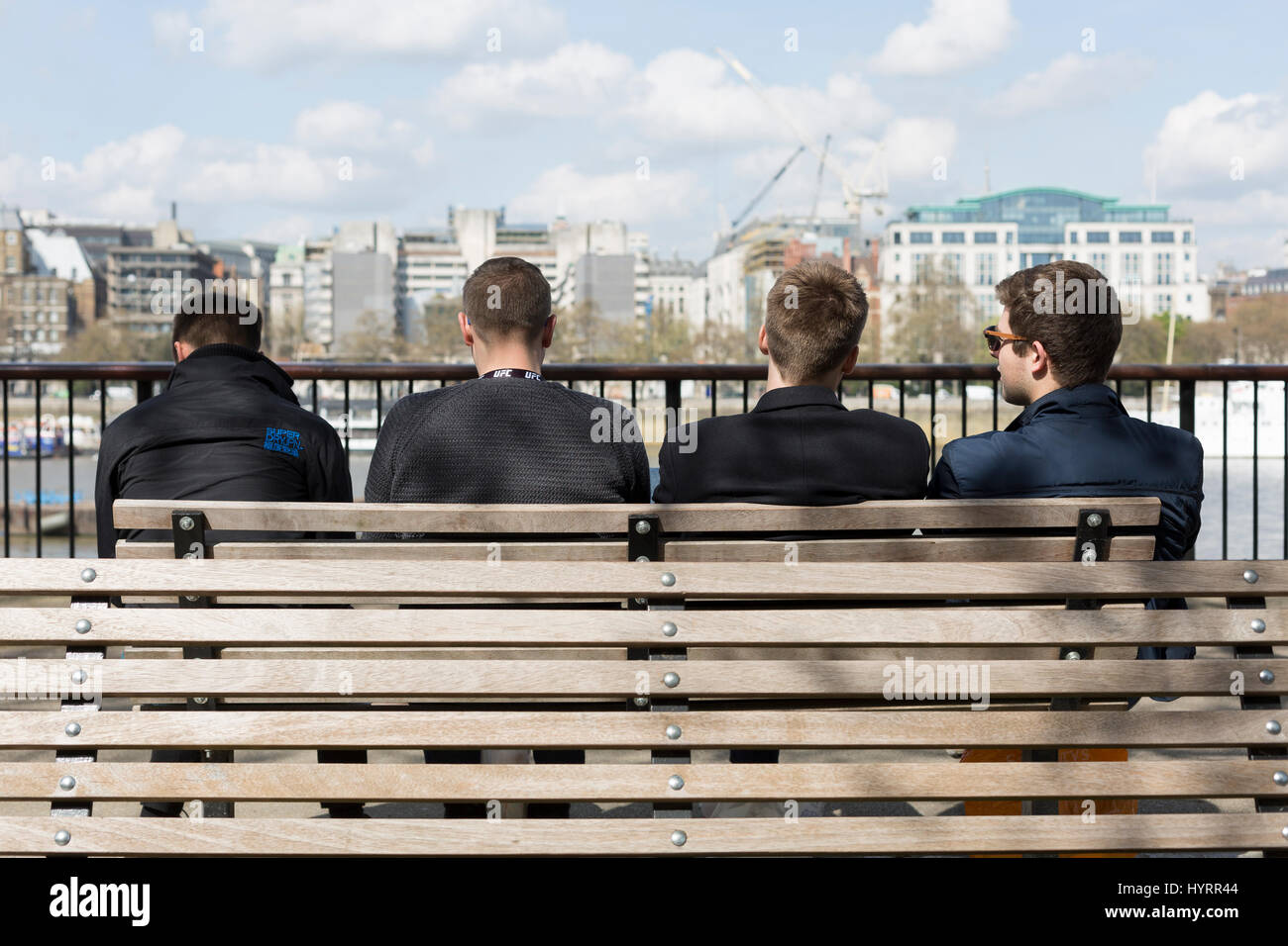 Four young men sit on bench with backs to the camera with London ...