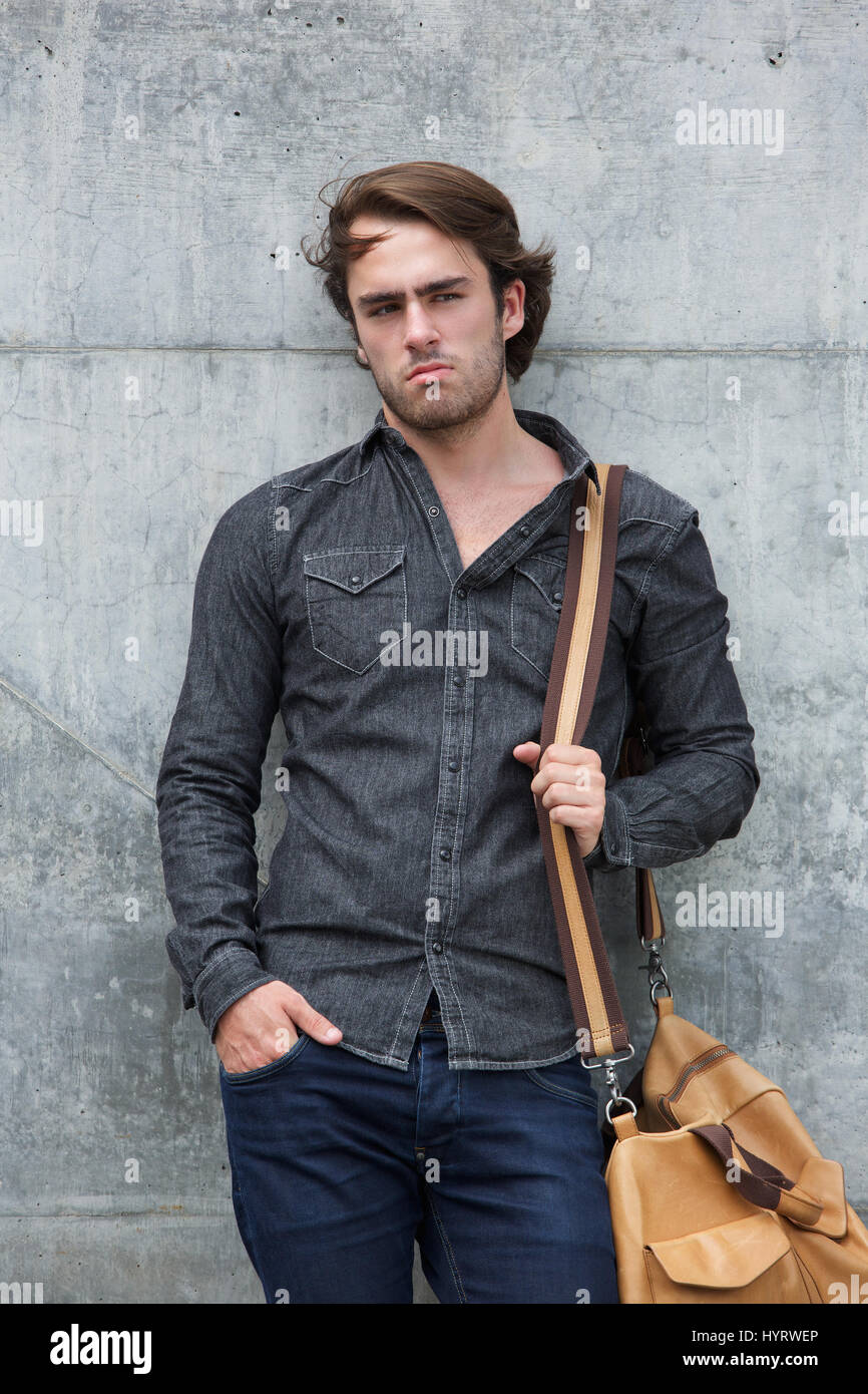 Portrait of a male model posing with leather travel bag outdoors Stock ...