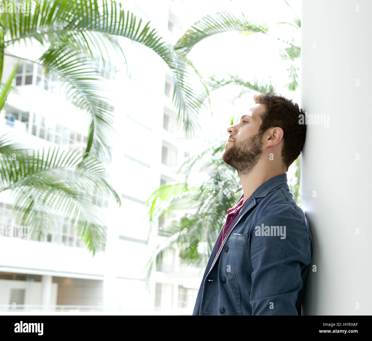 Side view portrait of a young man leaning against wall looking away ...