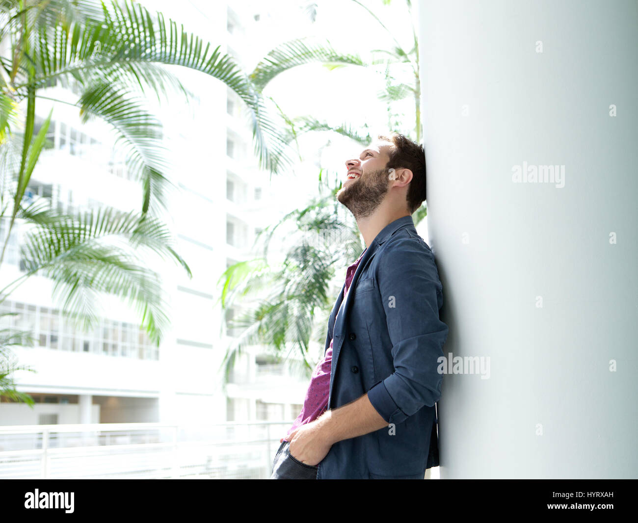 Profile portrait of a happy young man leaning against wall in bright ...