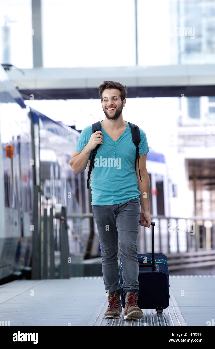 Full length portrait of a happy young man walking with suitcase at ...