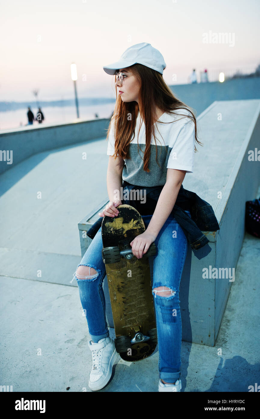 Young teenage urban girl with skateboard, wear on glasses, cap and ...